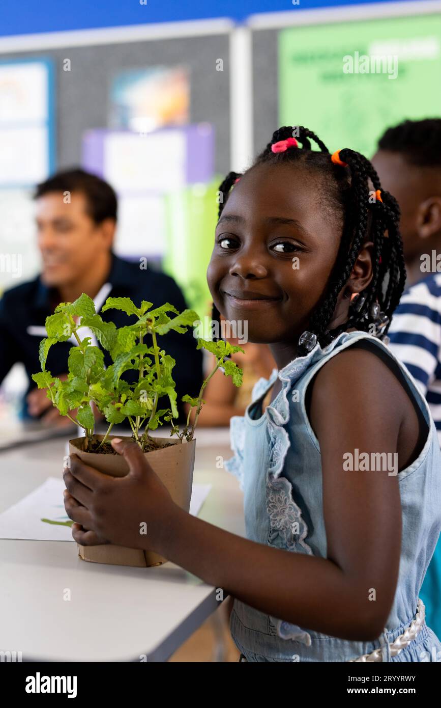 Portrait of happy african american girl with plant in ecology class at ...