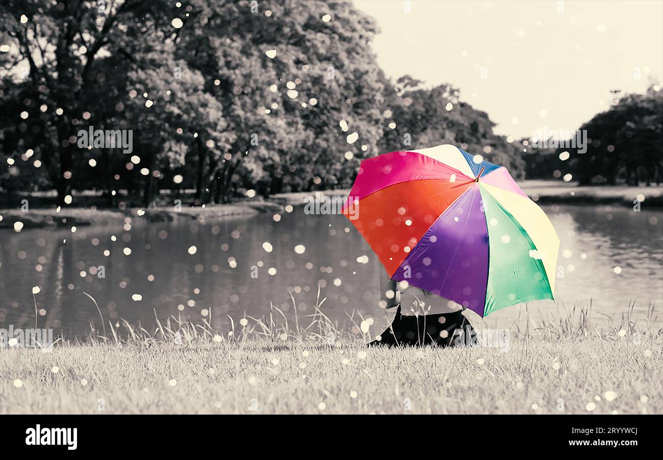 Colorful rainbow umbrella hold by sitting woman on grass field near ...
