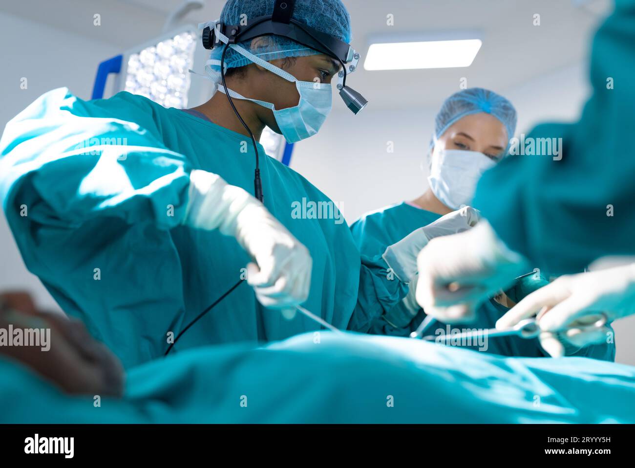 Diverse surgeons wearing surgical gowns operating on patient in ...