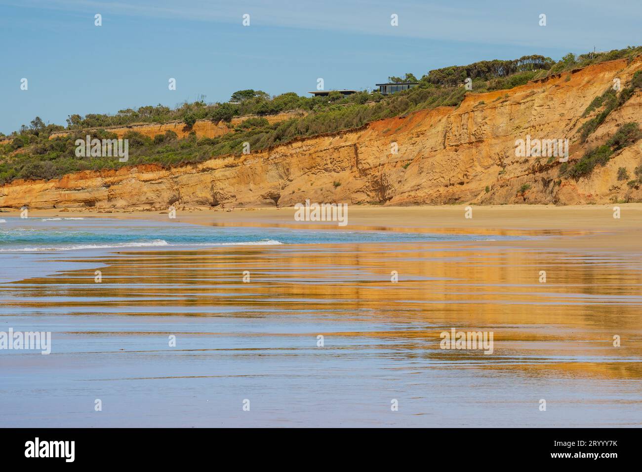 Low angled view of sea cliffs reflected on a wet sandy beach on the ...