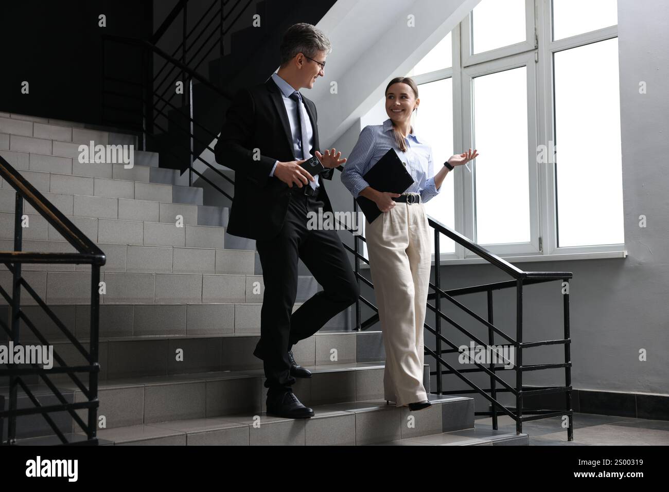 Coworkers talking while going down stairs in office Stock Photo - Alamy