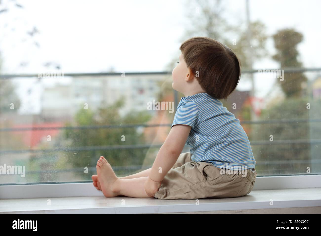 Little boy sitting on window sill. Child in danger Stock Photo - Alamy