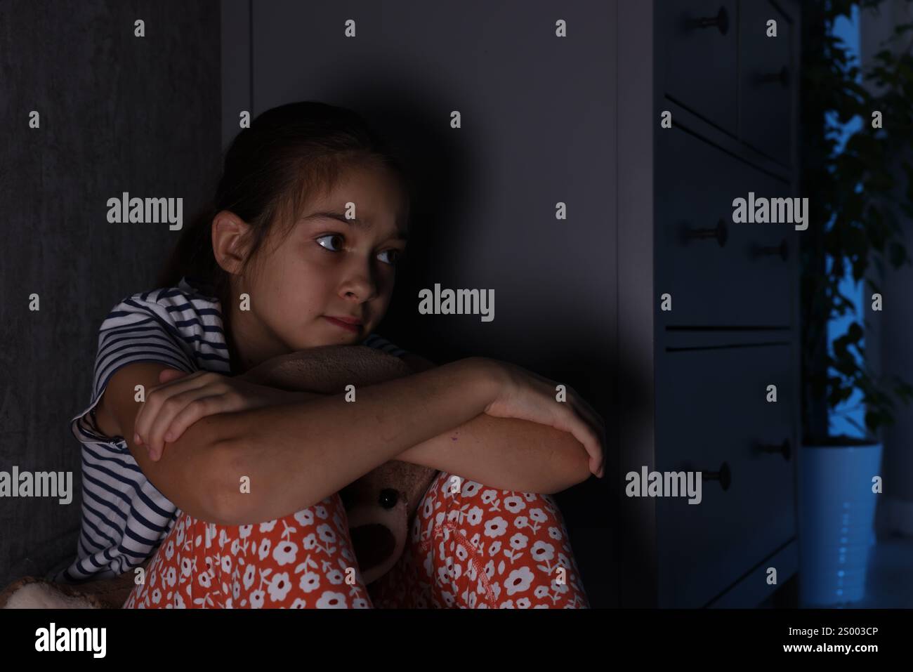 Scared girl with teddy bear hiding behind chest of drawers in her room ...