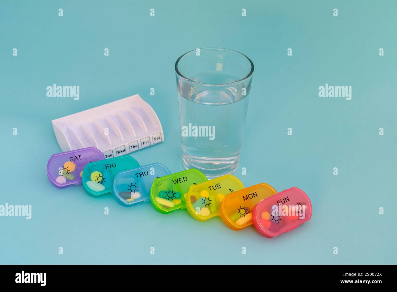 Pills in a plastic pill boxes for 7 days of a week with glass of water ...