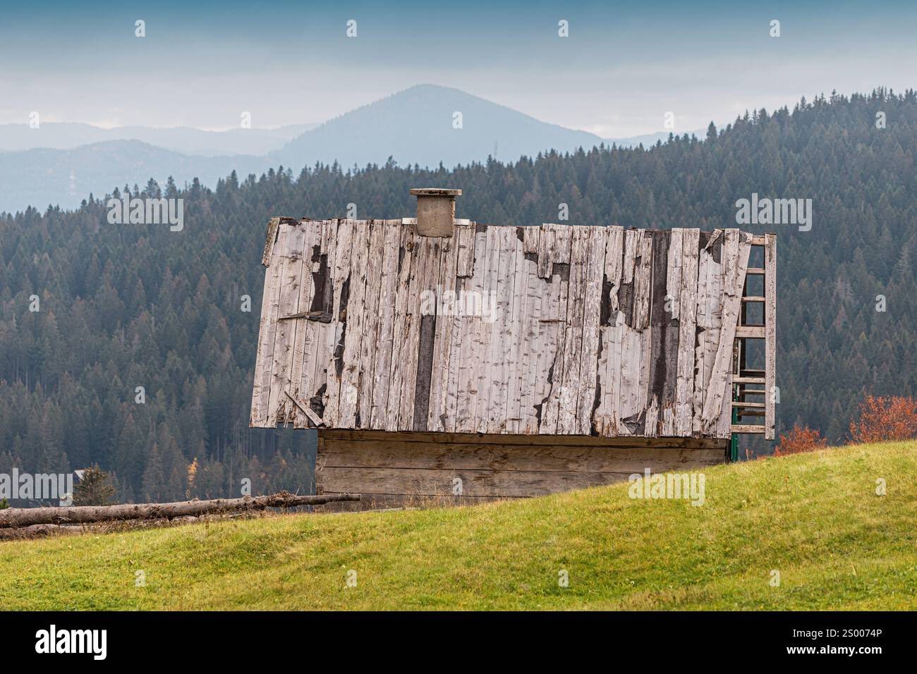 Weathered wooden cabin with decaying roof and chimney in the mountains ...