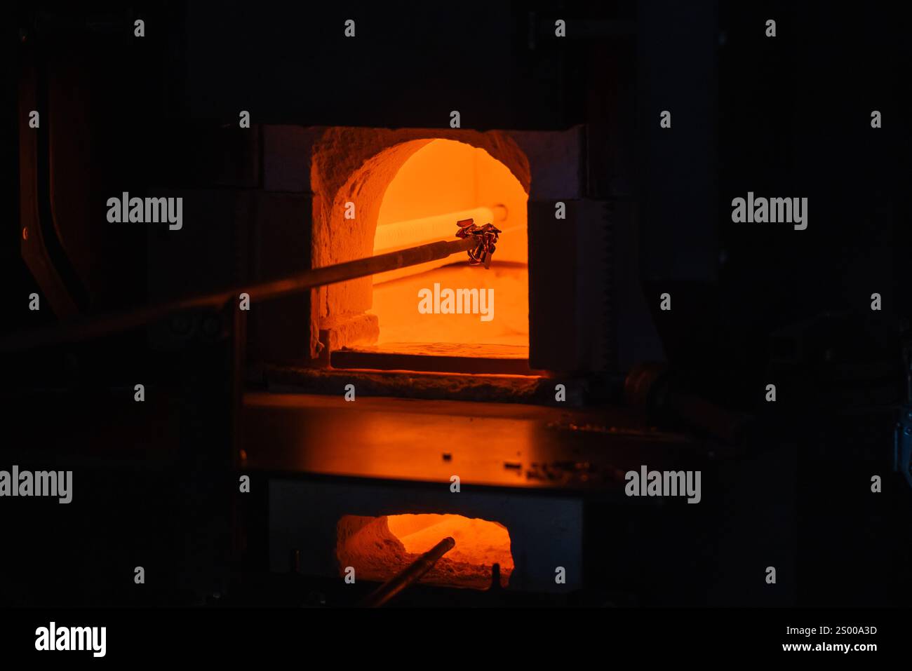Open furnace with molten glass on a blowpipe inside. Works of glass ...