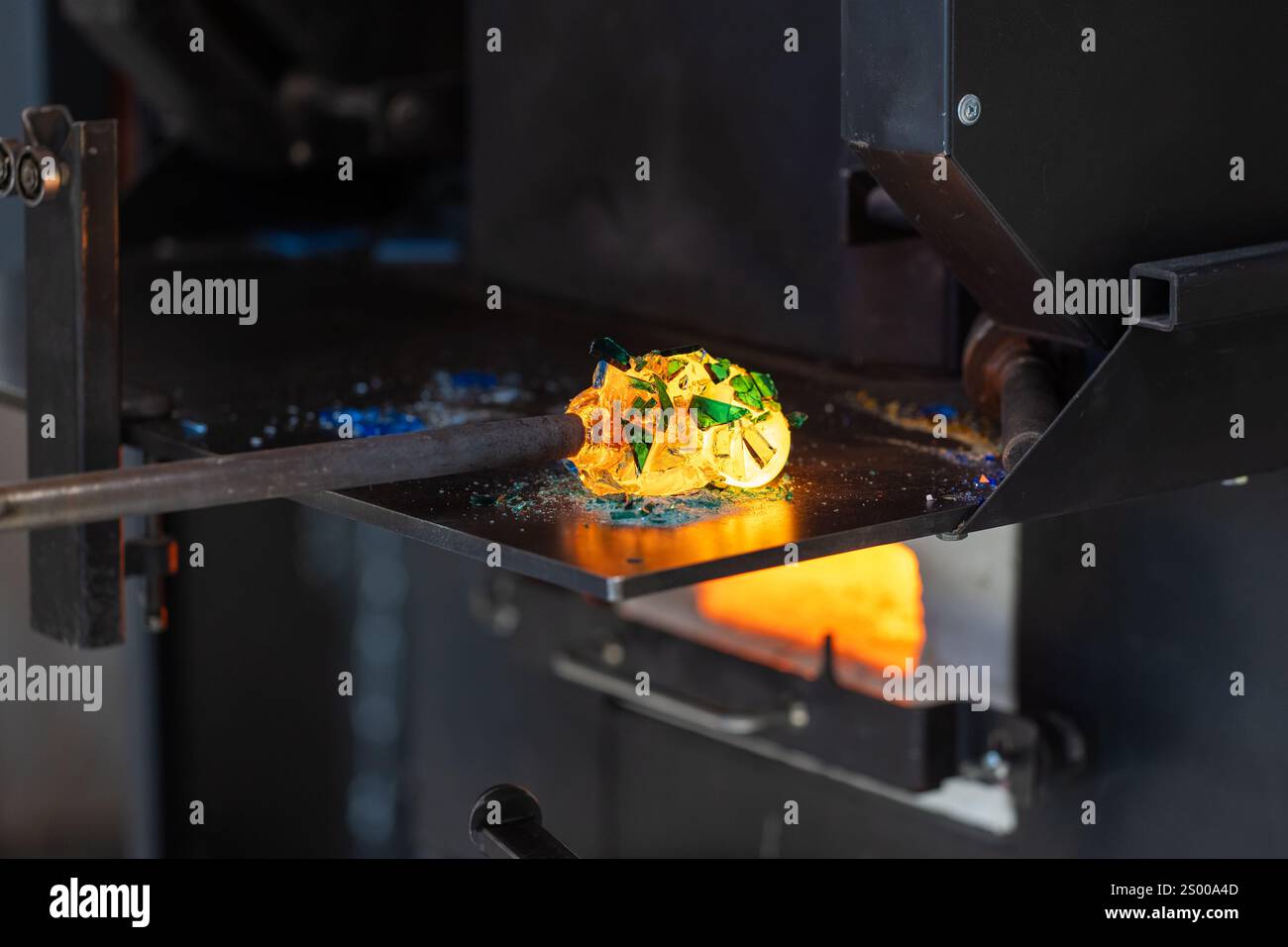 Molten glass fusing with colorful fragments on a blowing pipe, glass ...