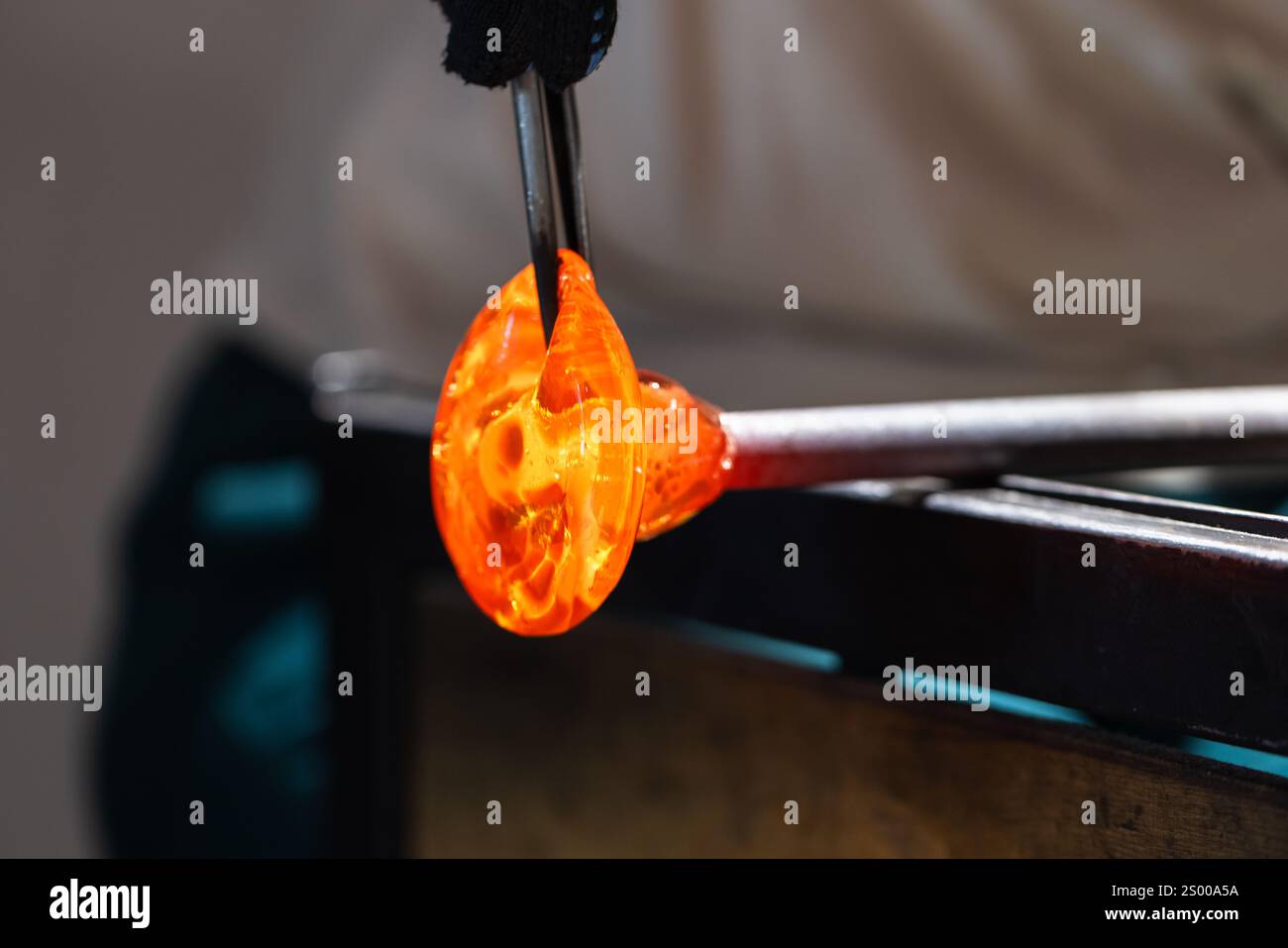 Molding red molten glass into a flower shape. Works of a glass blowing ...