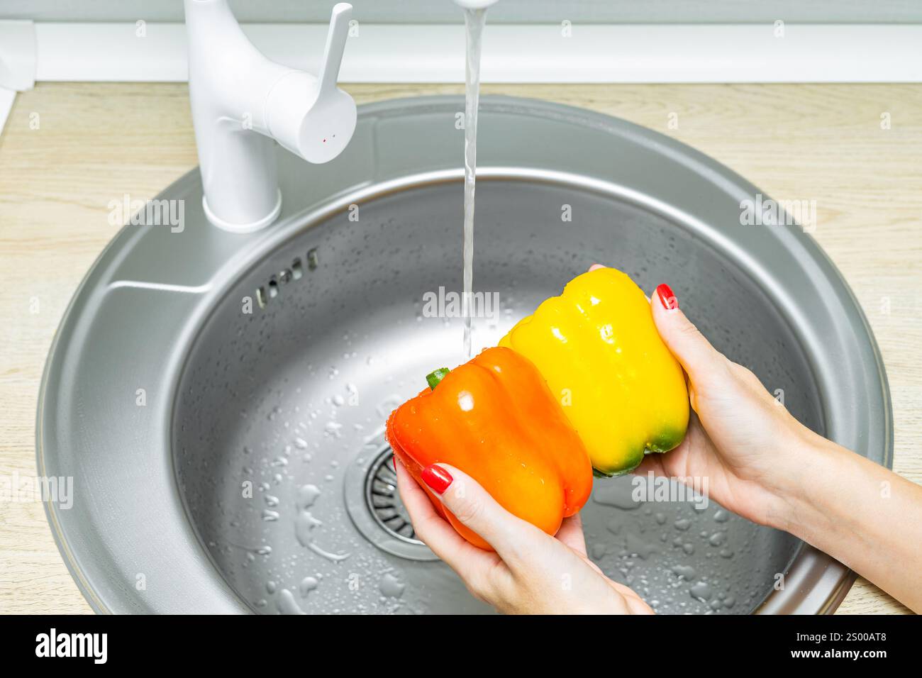 woman washing bell peppers in kitchen sink. housewife washes vegetables ...