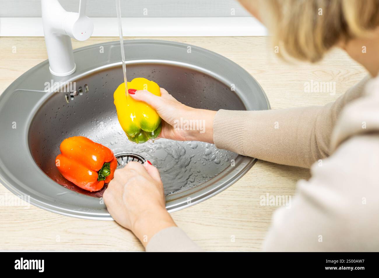 woman washing bell peppers in kitchen sink. housewife washes vegetables ...