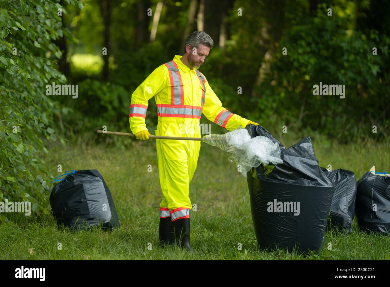 Volunteer in rubber gloves with trash bag clean up garbage on forest outdoor. Eco, environment ...