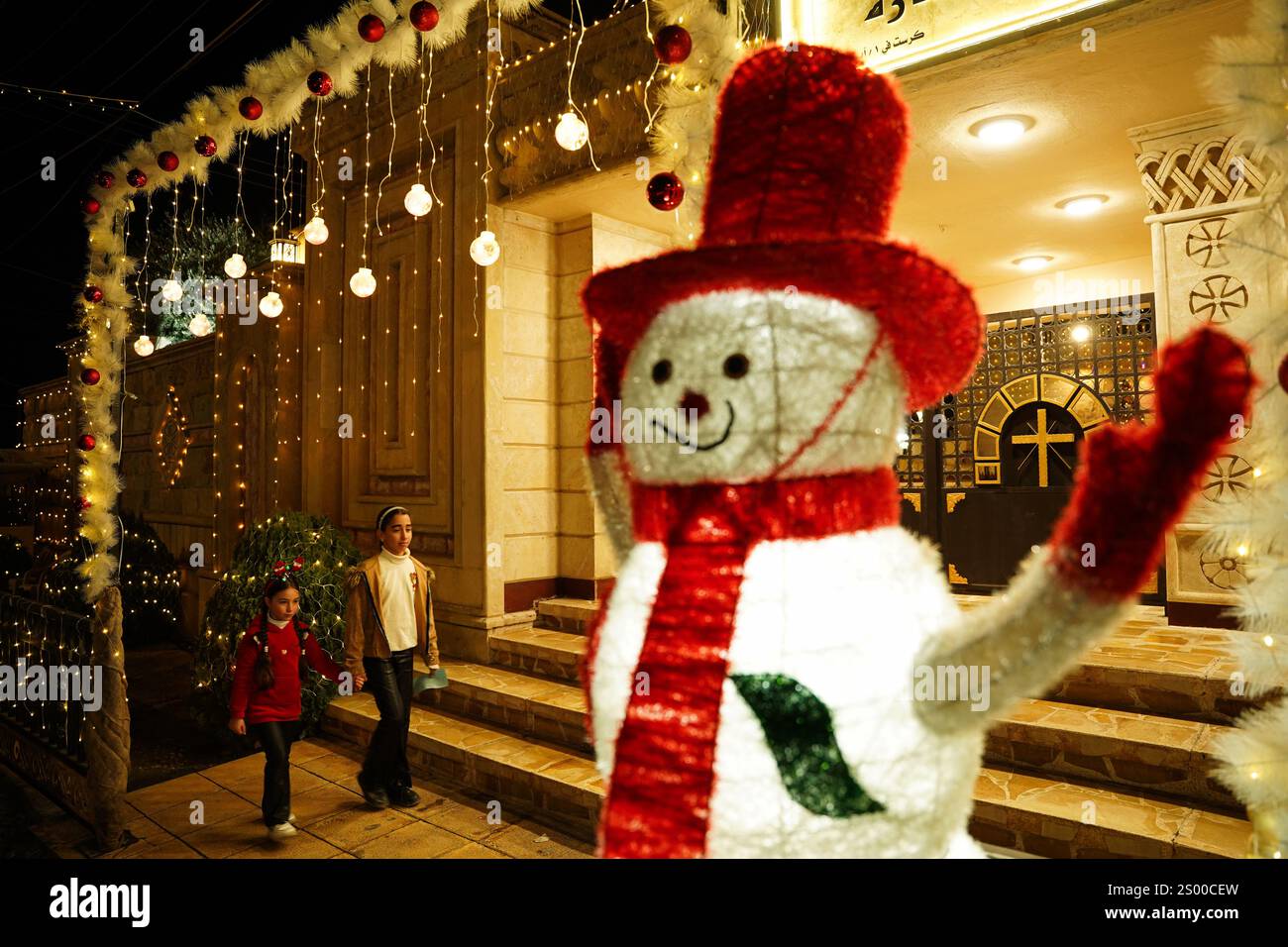 Christians walk through decorated streets in the town of Qaraqosh, also ...