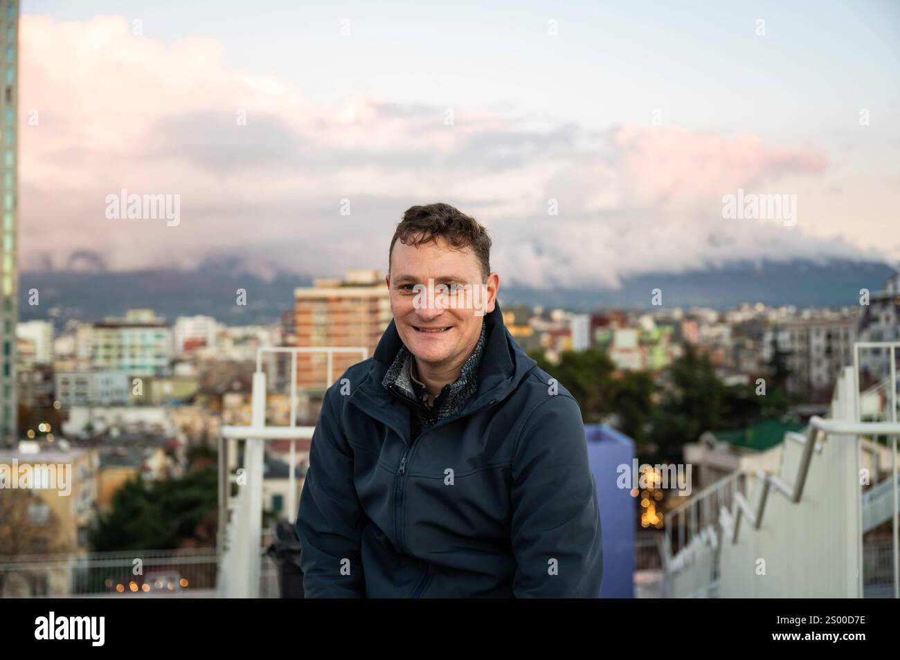 Portrait of a smiling 45 yo man with the city of Tirana at dusk in the ...