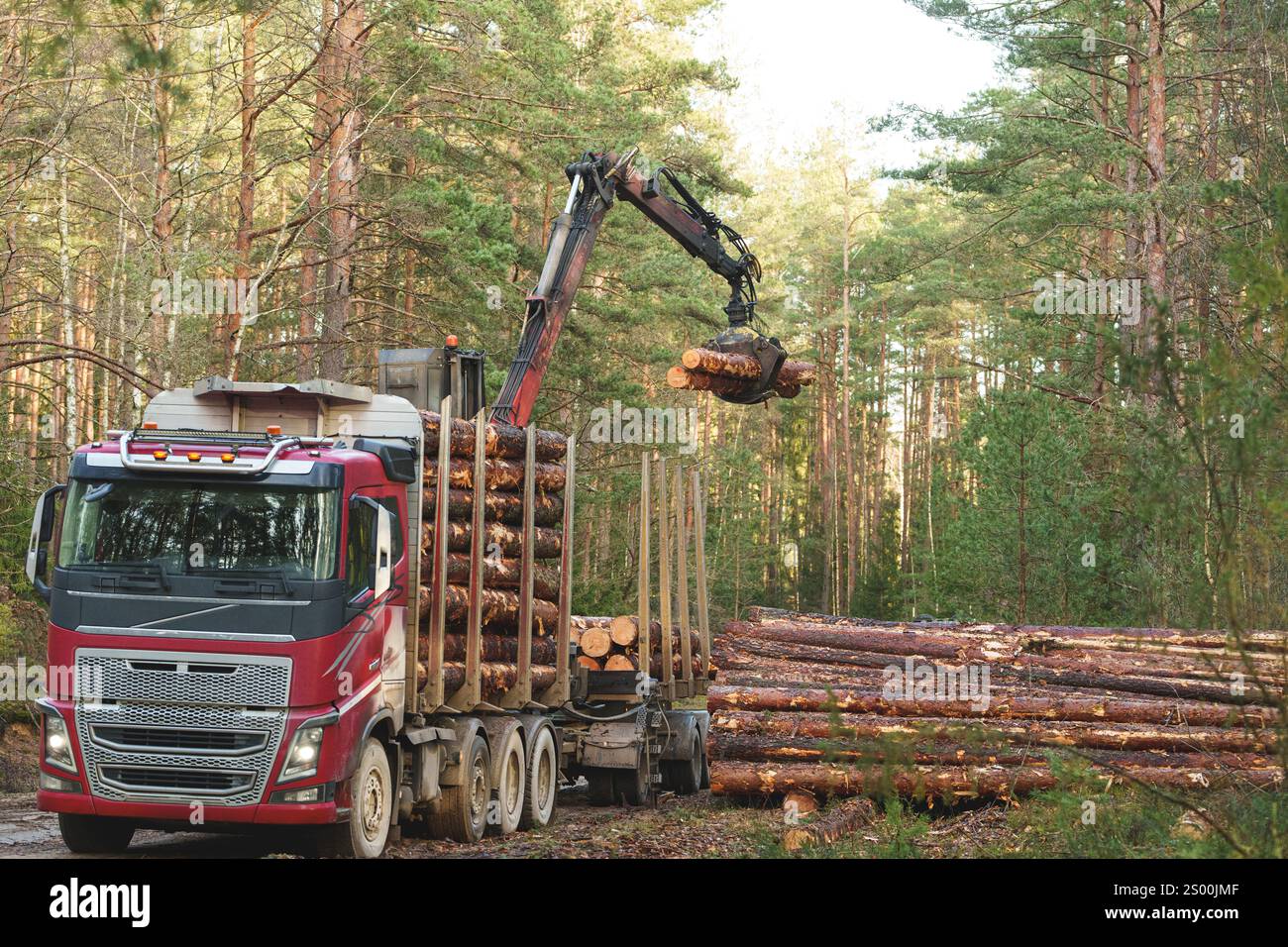 A red logging truck is being loaded with logs by a mechanical crane in ...
