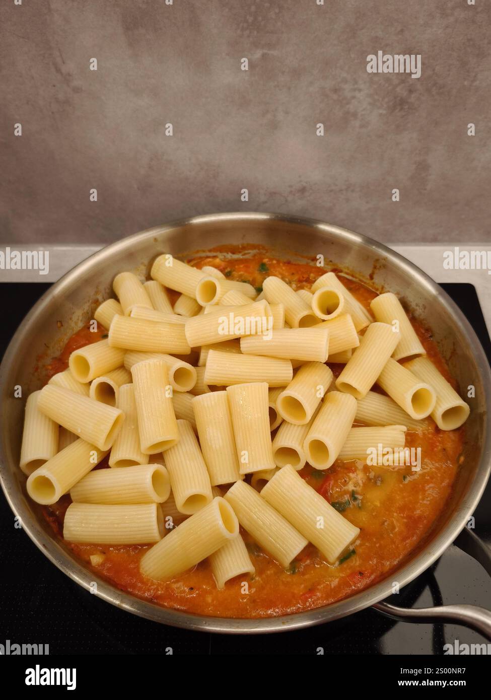 Rigatoni pasta added to tomato sauce in stainless steel pan Stock Photo ...