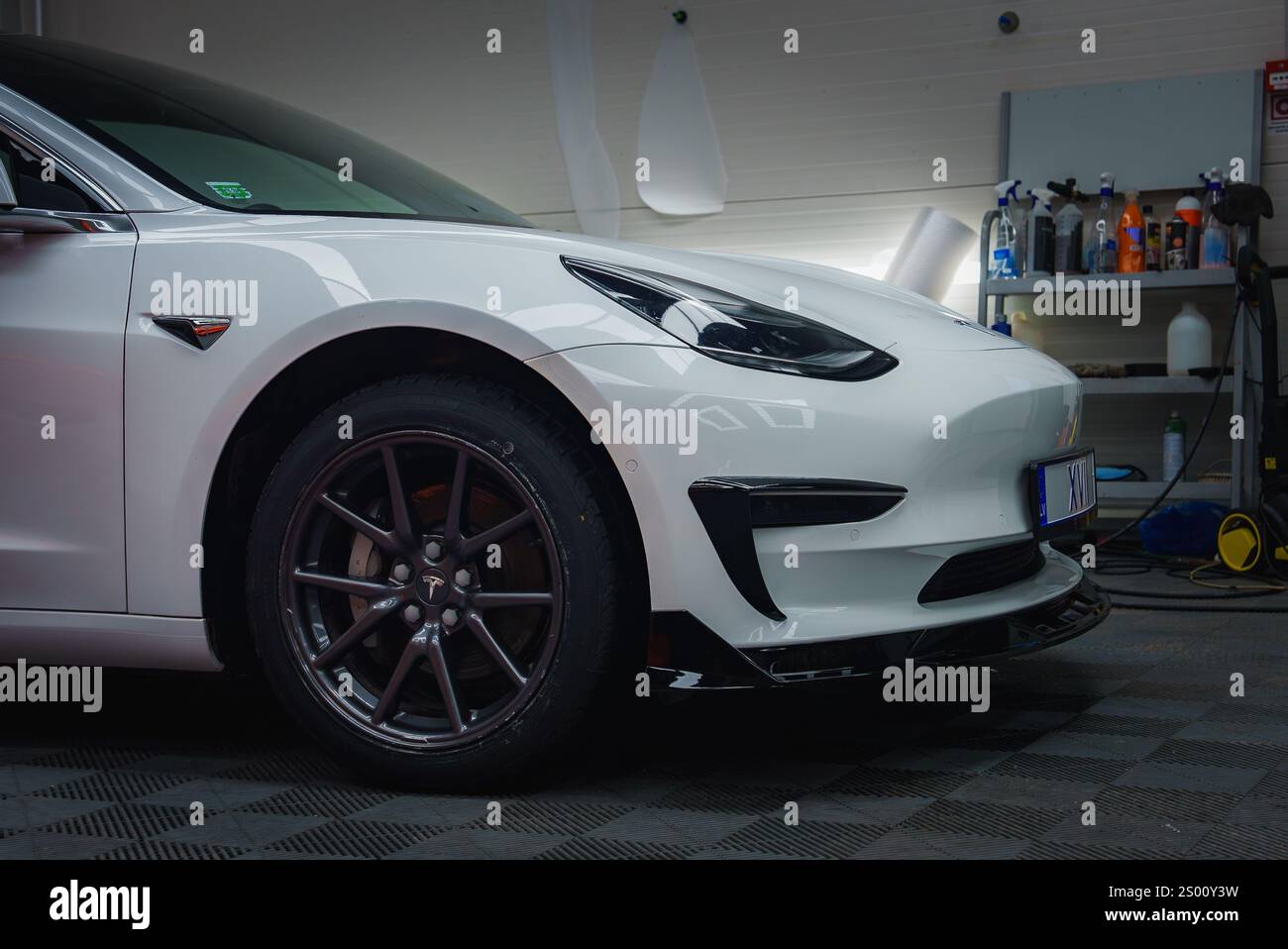 A white Tesla vehicle is shown indoors, focusing on the front left side ...