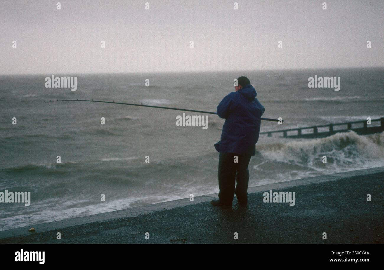 A solitary angler fishing from a sea wall in Hythe Kent on a cold and ...
