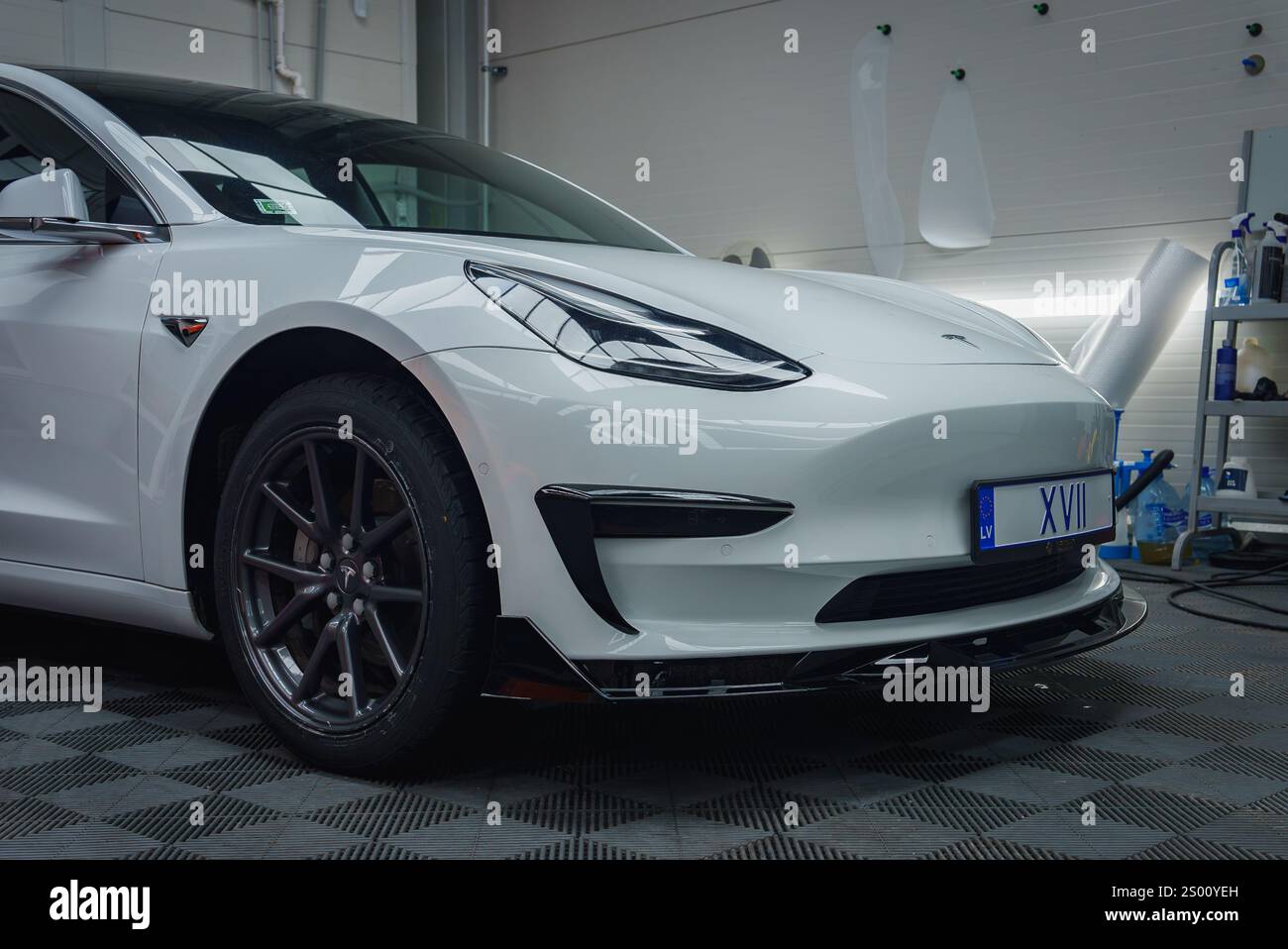 A white Tesla Model 3 is parked indoors on a checkered floor ...