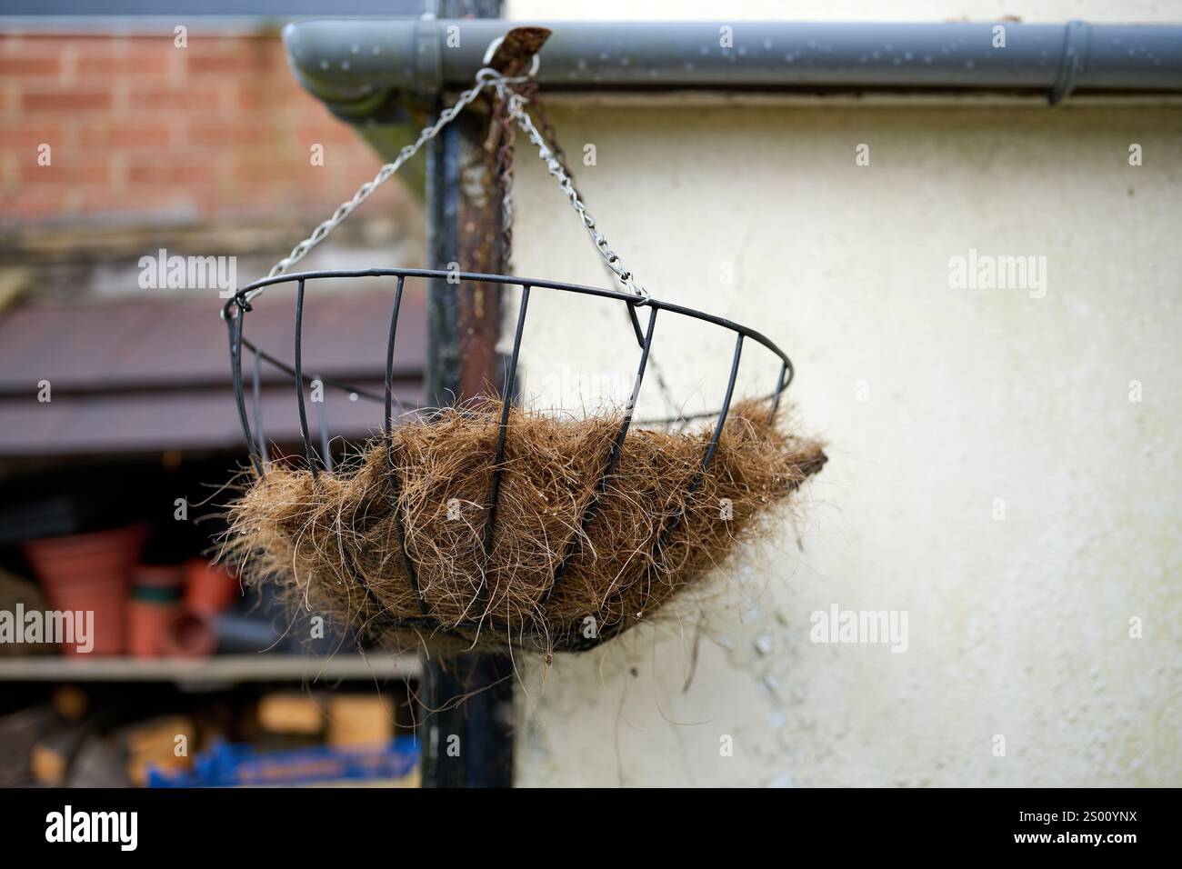 Empty hanging flower basket with natural liner against a wall ...