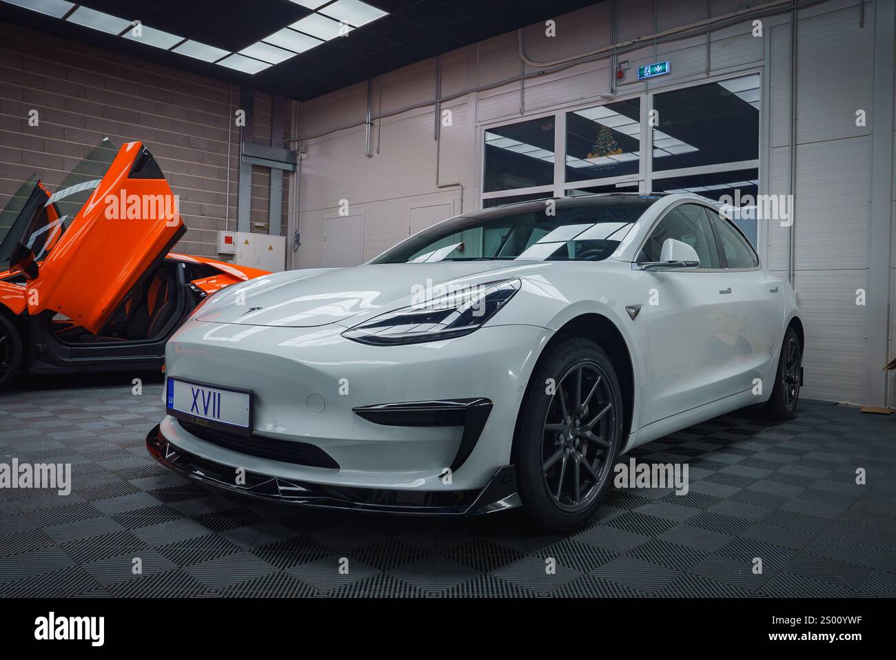 White Tesla Model 3 and Orange Lamborghini in Modern Showroom Stock ...