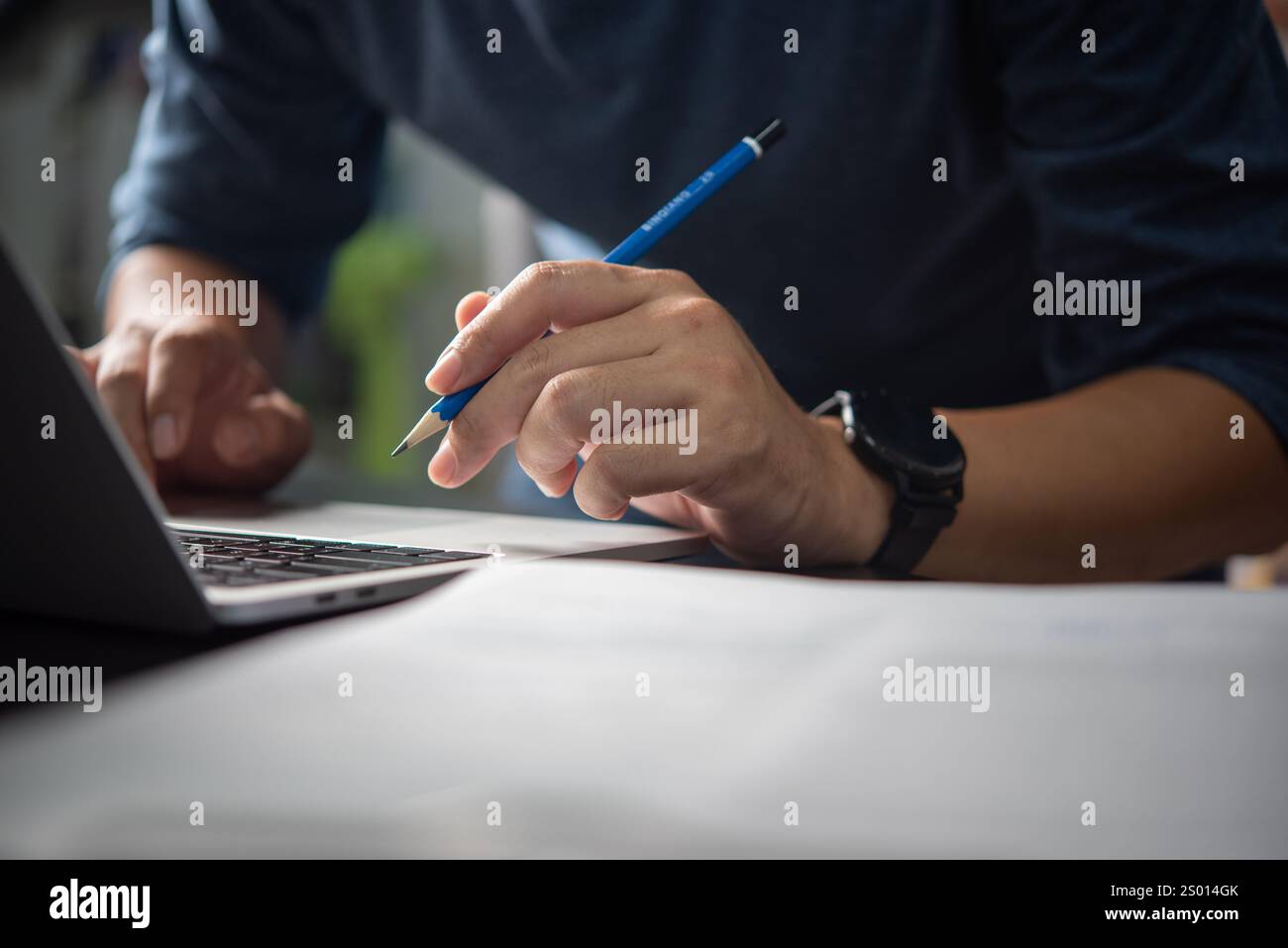 Person holding pencil while typing on a laptop, focused on work ...