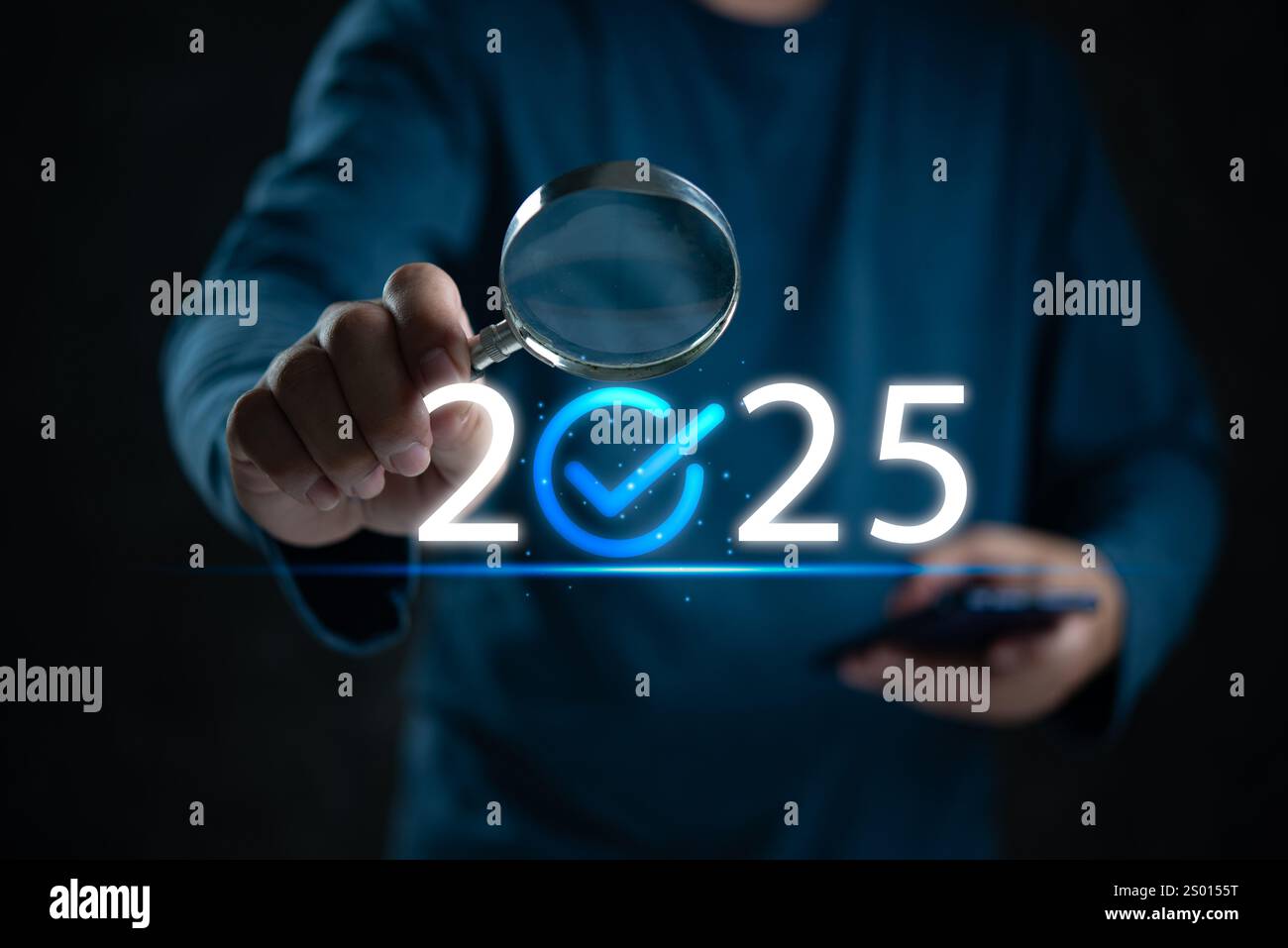 Hand holding a magnifying glass over the year 2025, representing ...