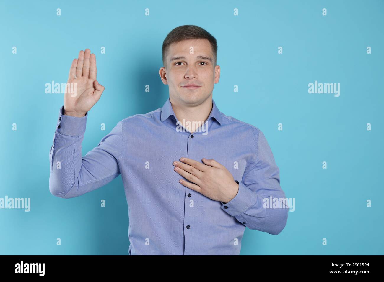 Man making promise with raised hand on light blue background. Oath ...