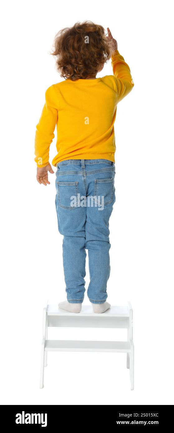 Little boy standing on step stool against white background, back view ...