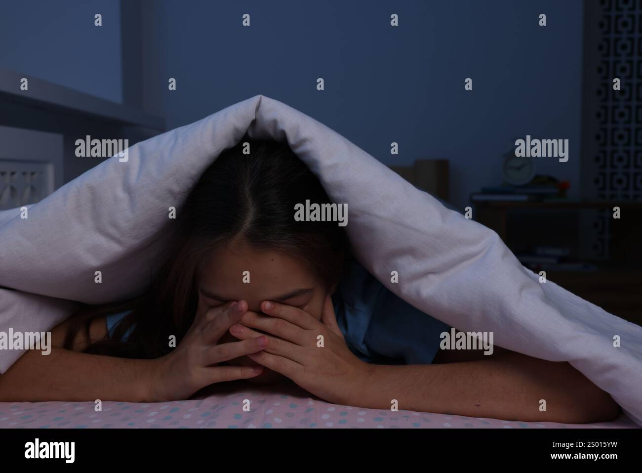 Afraid girl hiding under duvet on bed at night Stock Photo - Alamy