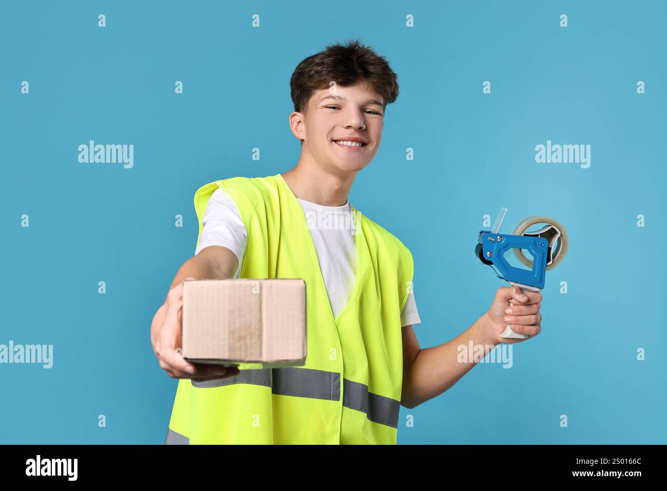 Teenage boy with tape gun dispenser and box in safety vest working as ...
