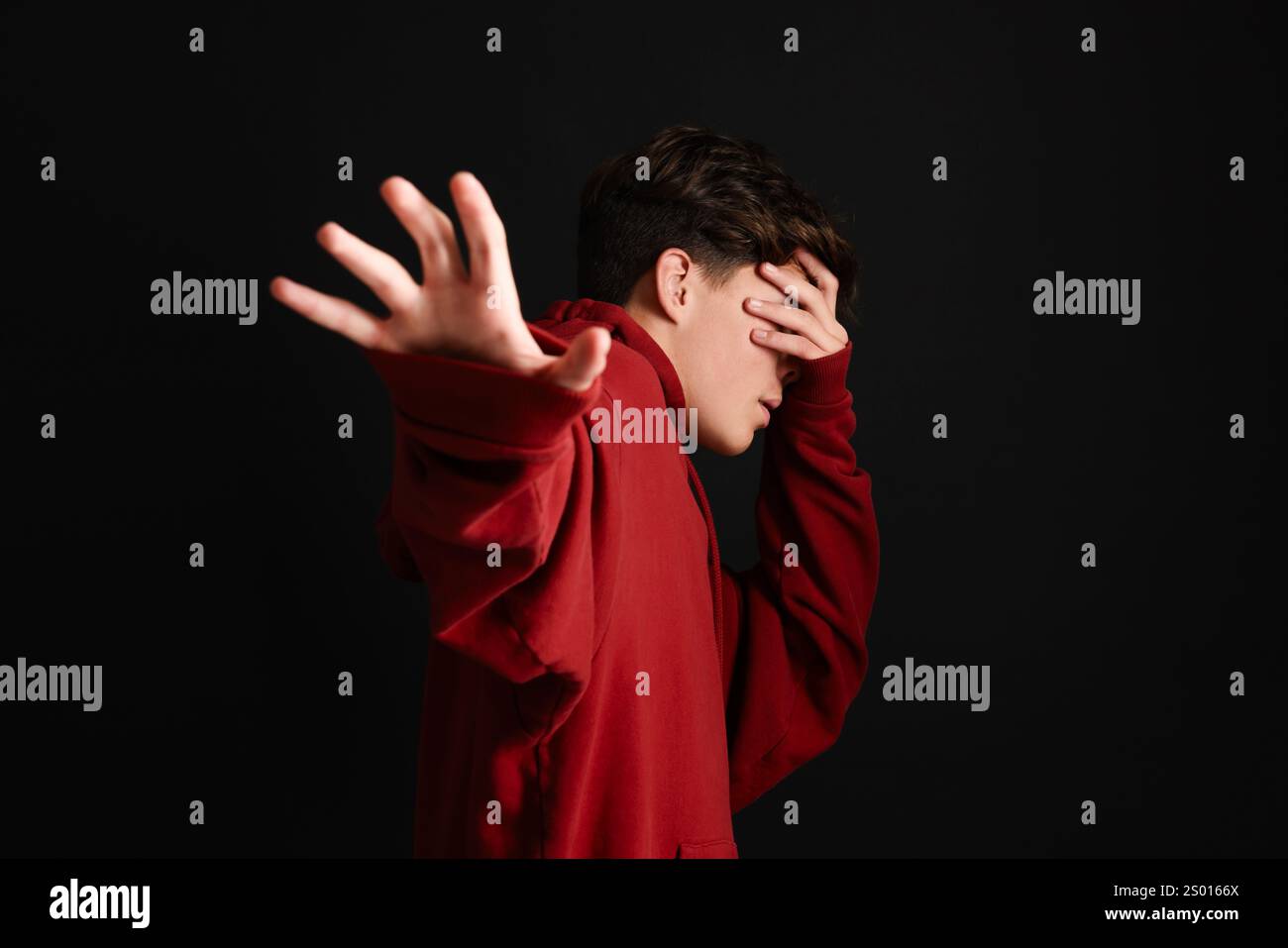 Scared teenage boy covering face with hands on black background Stock ...
