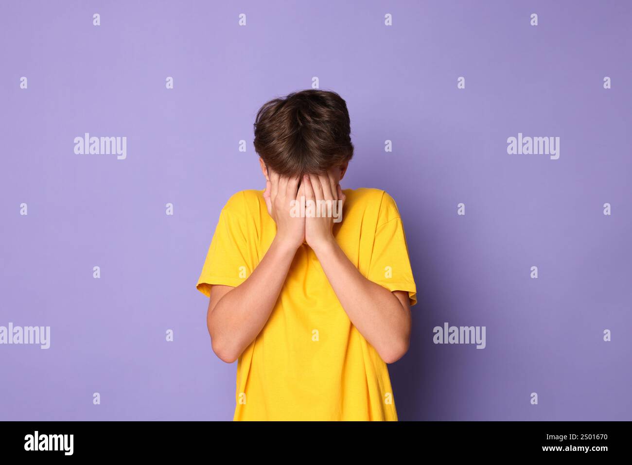 Scared teenage boy covering face with hands on violet background Stock ...