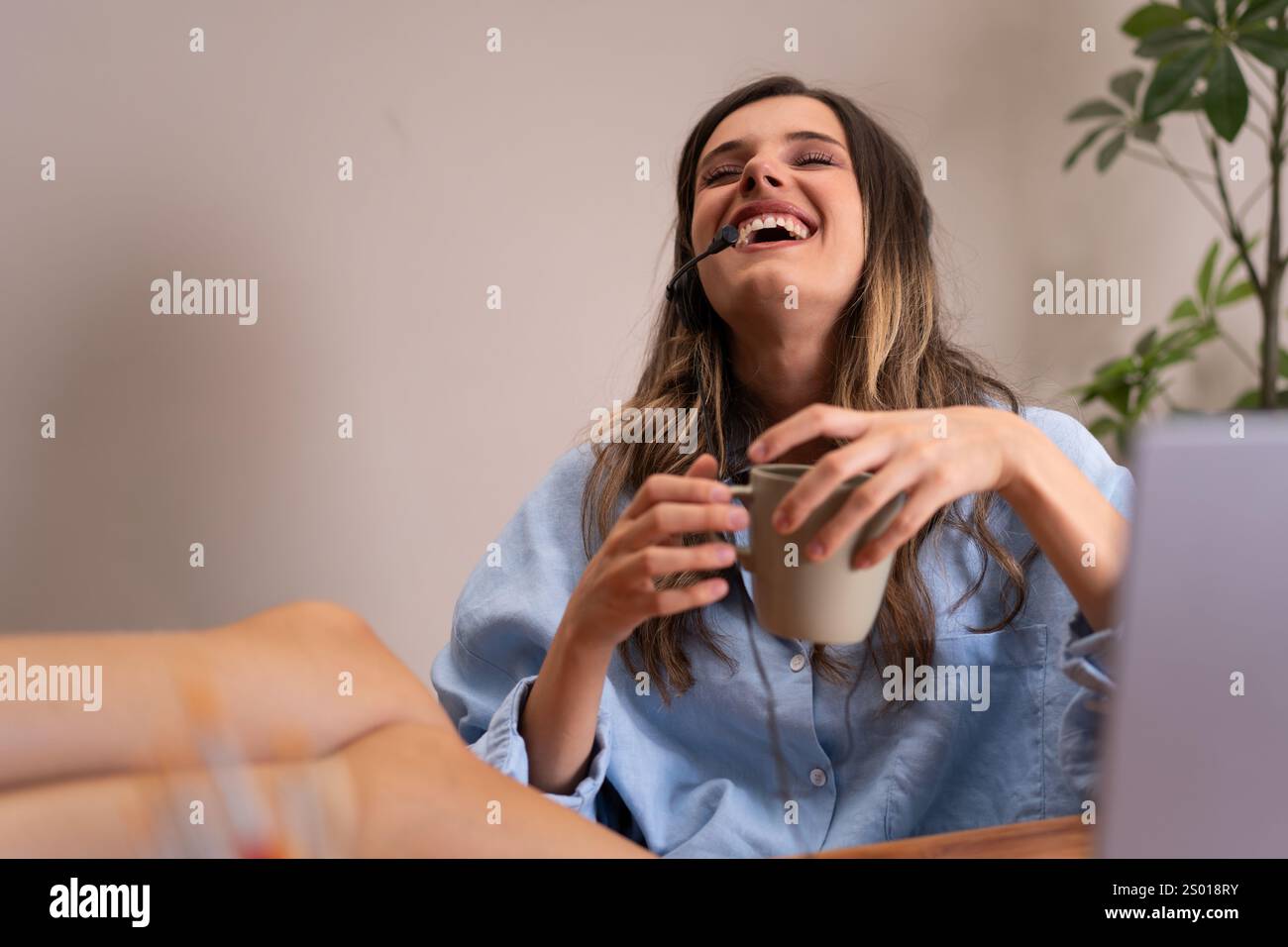 A cheerful woman wearing a headset, laughing and enjoying a coffee ...