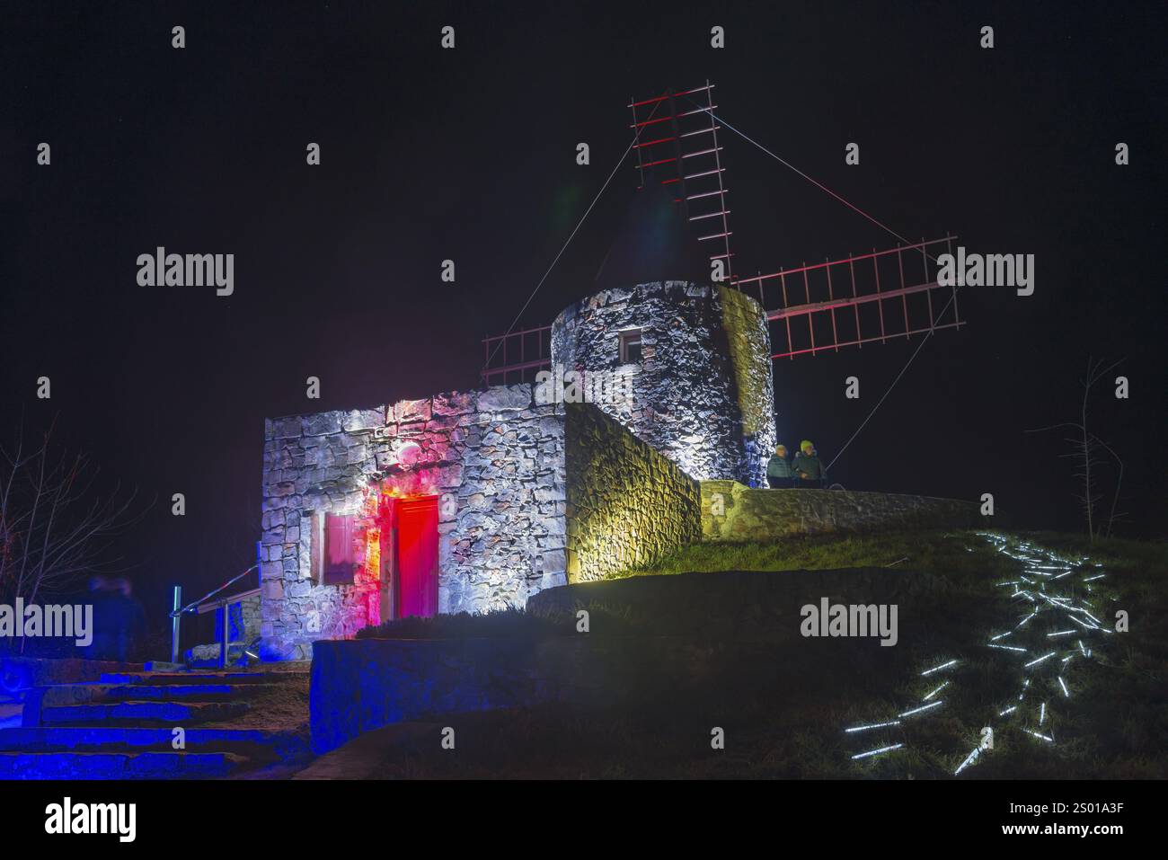 Old windmill on an illuminated hill at night, highlighted by red and ...