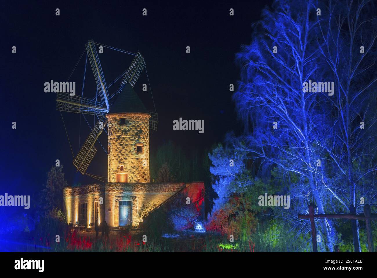 Historic stone mill at night, illuminated in blue, surrounded by trees ...