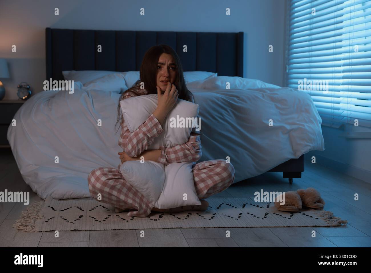 Fear of darkness. Scared young woman hugging pillow in bedroom at night ...