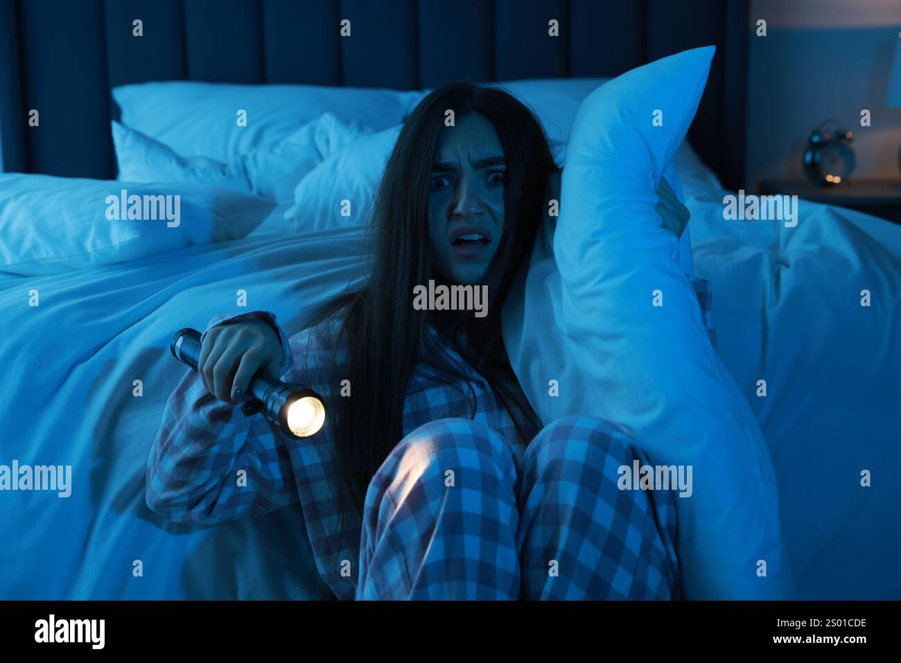 Fear of darkness. Scared young woman with flashlight hugging pillow in ...