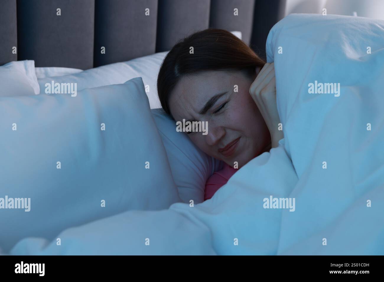 Fear of darkness. Scared young woman lying on bed in room at night ...