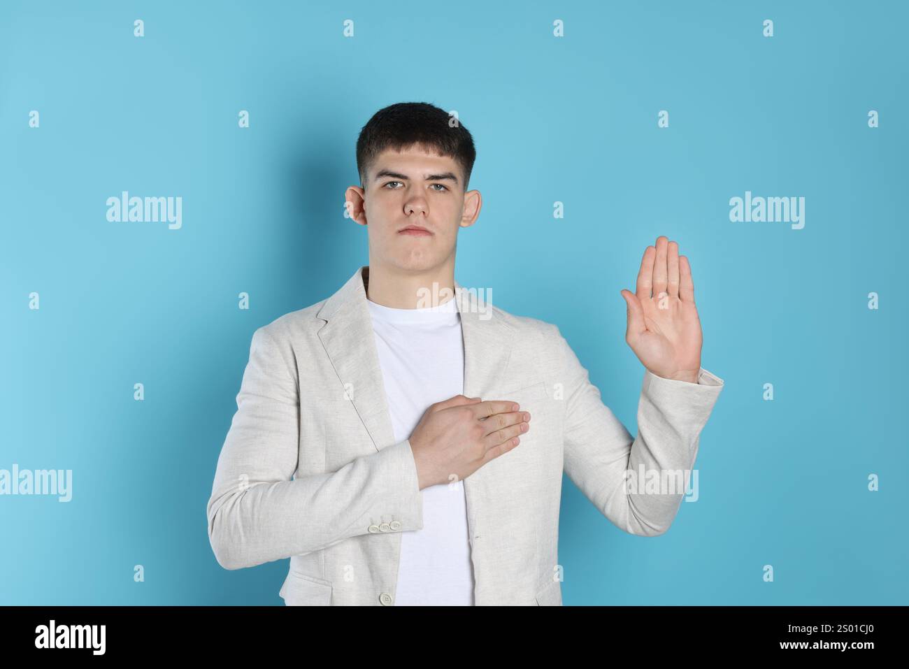 Man making promise with raised hand on light blue background. Oath ...