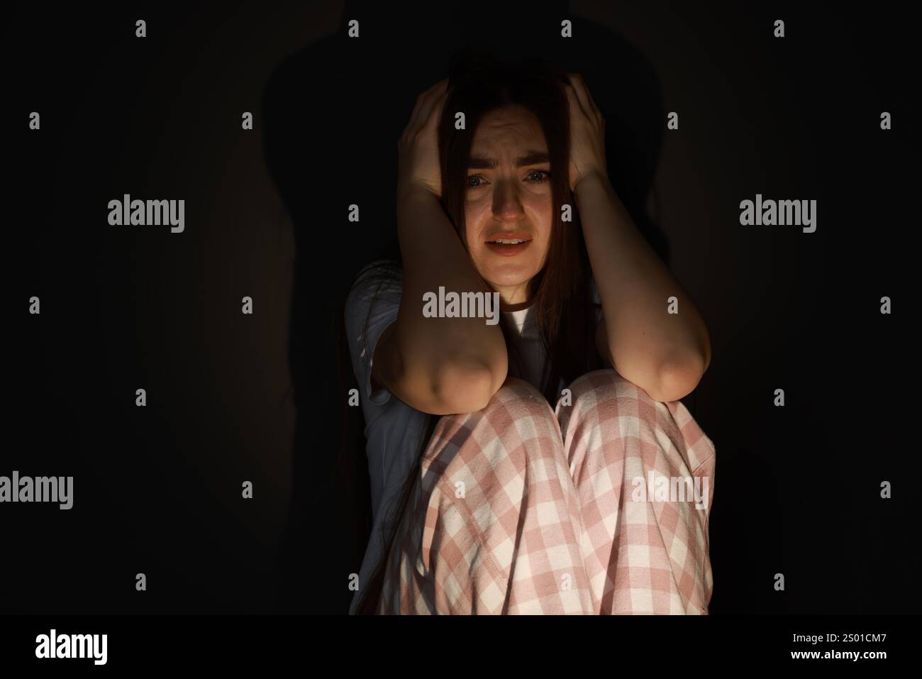 Fear of darkness. Scared young woman sitting on dark background Stock ...
