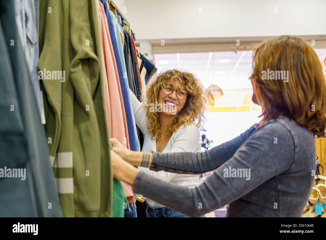 Two joyful female customers browsing through colorful clothes on ...