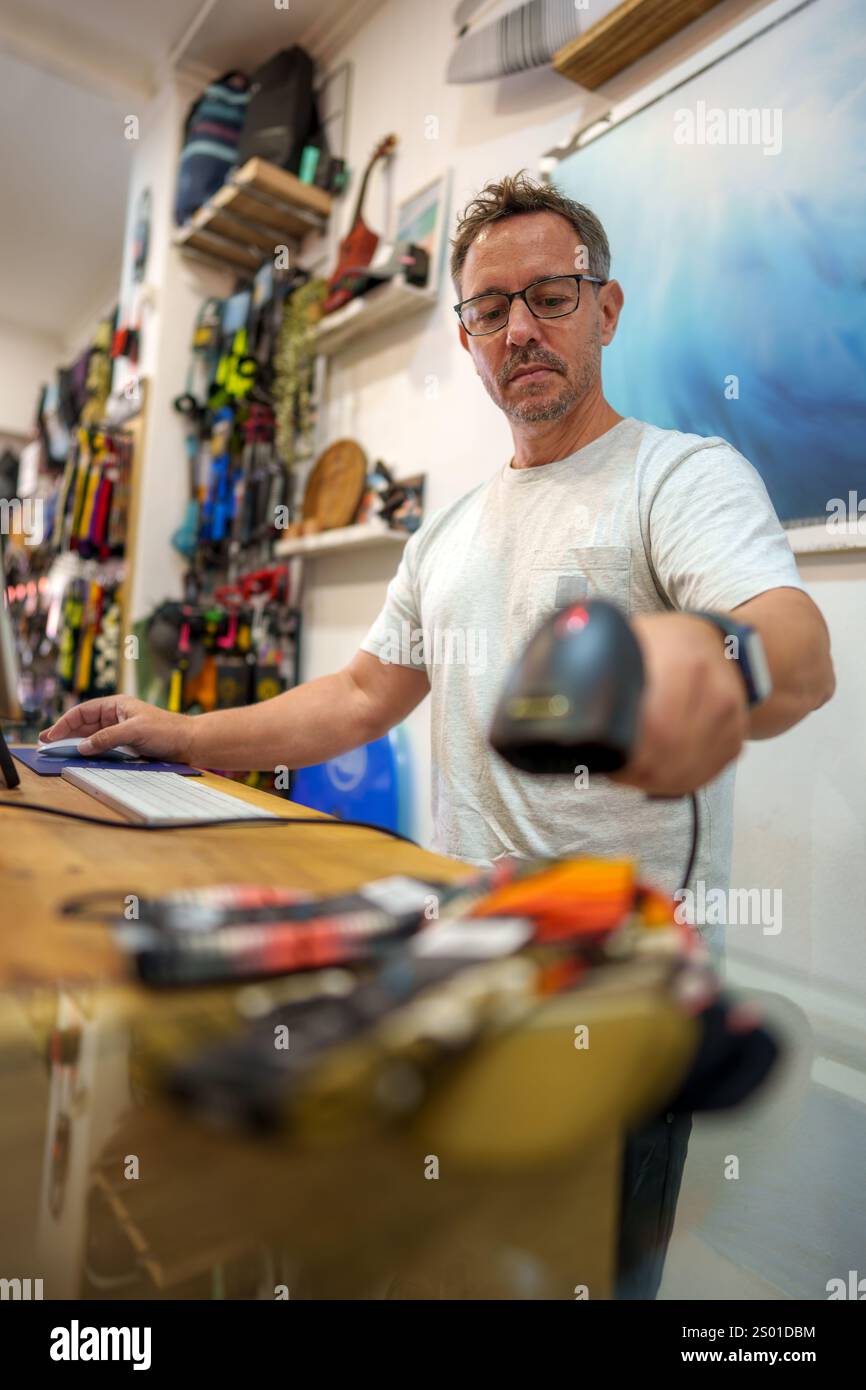 Mature male shopkeeper scanning products with barcode reader while ...