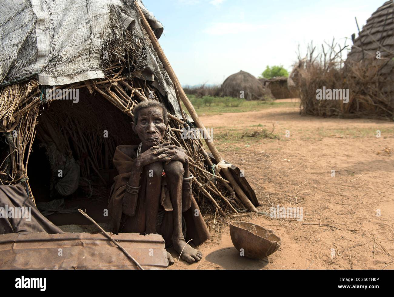Old emaciated woman marked by her age sitting in front of her conical ...