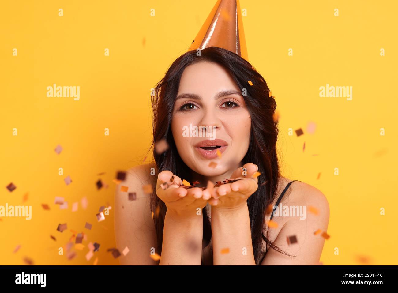 Beautiful woman in conical paper hat blowing confetti off hands on ...