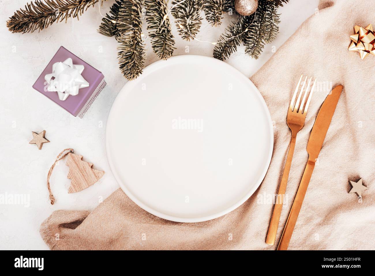 Flat lay of festive table setting with blank plate, gold cutlery, pine ...