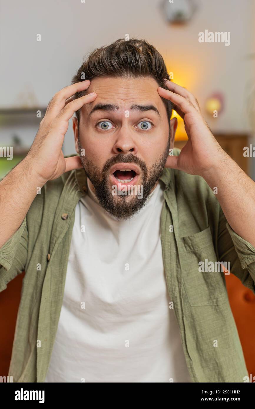 Shocked Caucasian young man with brown hair watching TV feeling ...