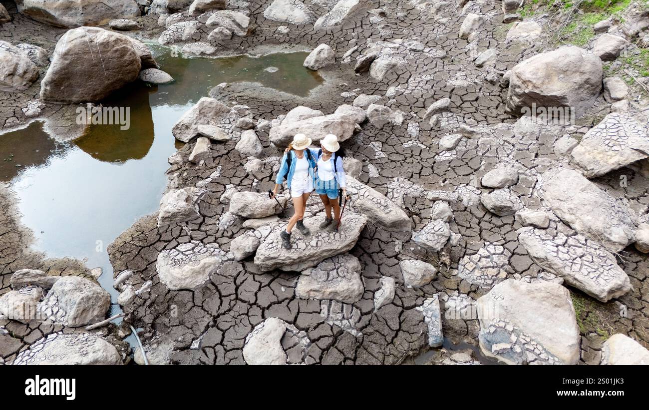Two hikers navigate a rugged terrain of dried mud and rocks, showcasing ...