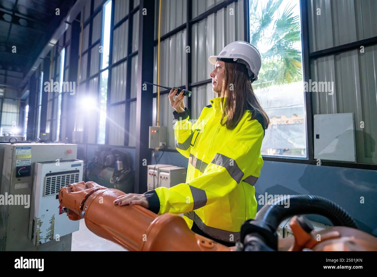 A worker wearing a safety helmet and bright jacket uses a walkie-talkie ...