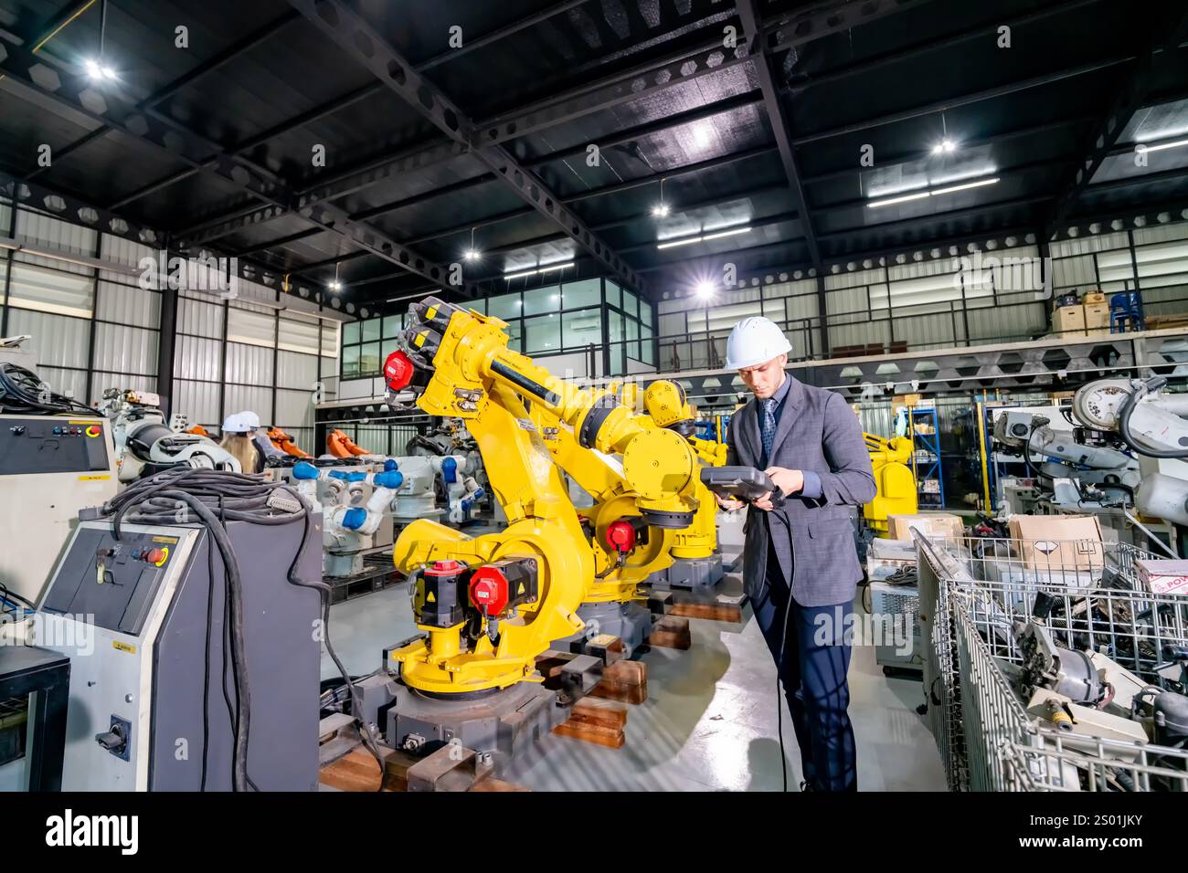 An engineer in a suit examines a yellow robotic arm inside a spacious ...