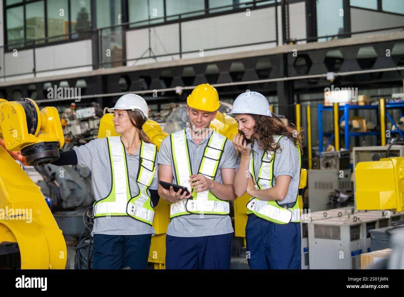Three team members in safety gear examine a tablet while standing near ...